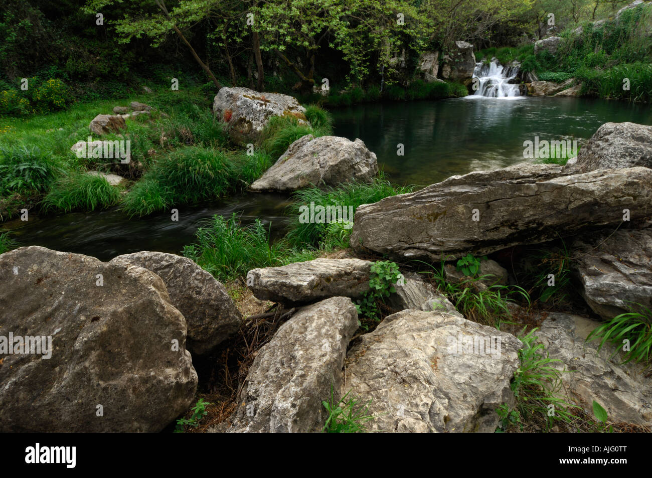 Image shows a small lake with a waterfall in the background and rocks ...