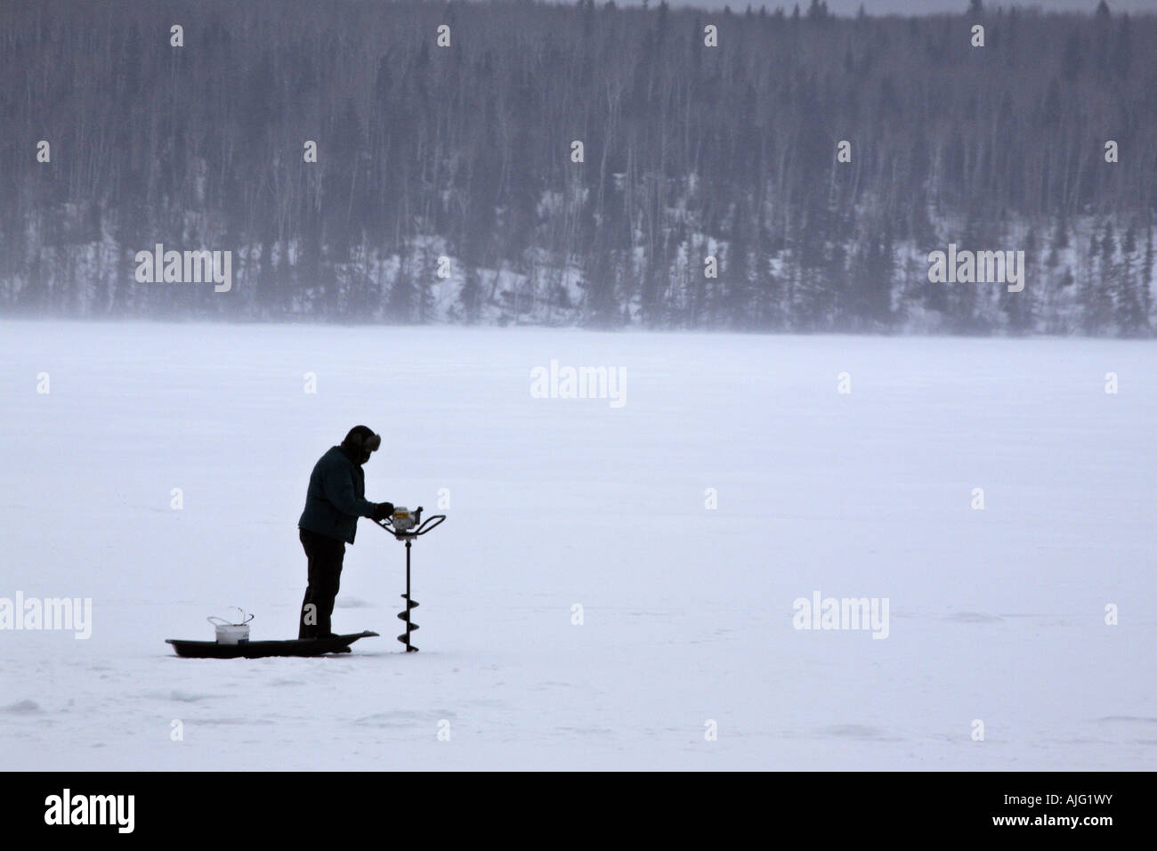 Fisherman drilling hole in ice Stock Photo - Alamy