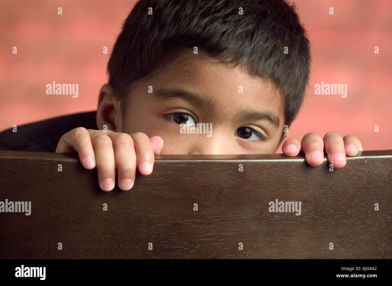 Portrait little Asian American boy peeking over back of chair Stock ...