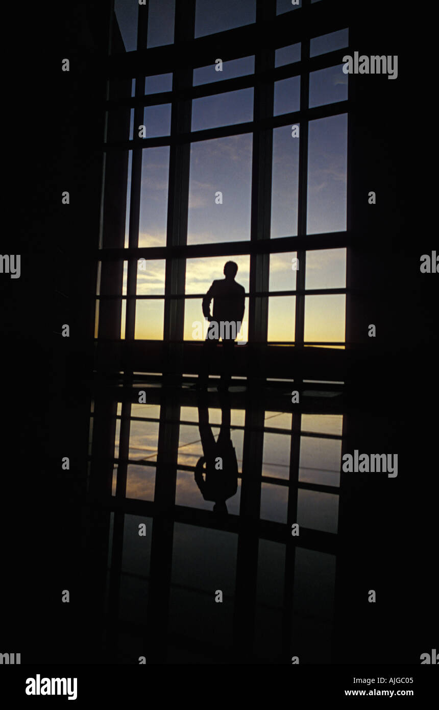 Silhouetted man gazing out big lobby window Stock Photo - Alamy