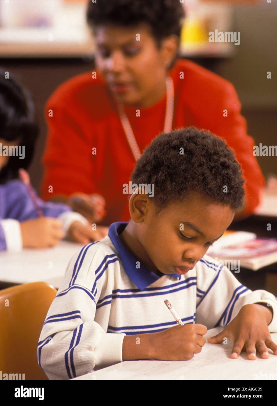 African American student writing in notebook at his desk in elementary ...