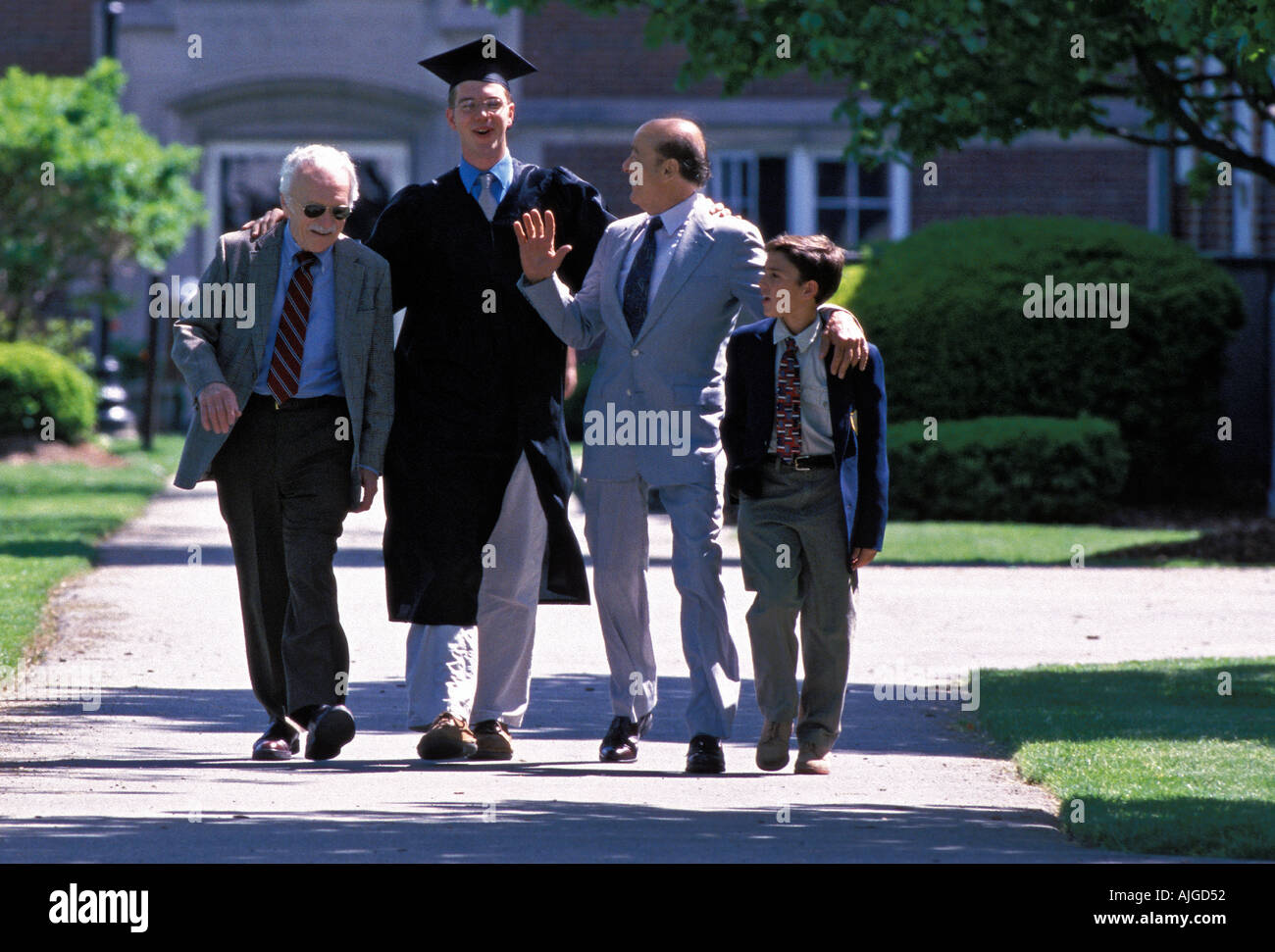 Caucasian male graduate walking with Dad Grandfather and brother on ...