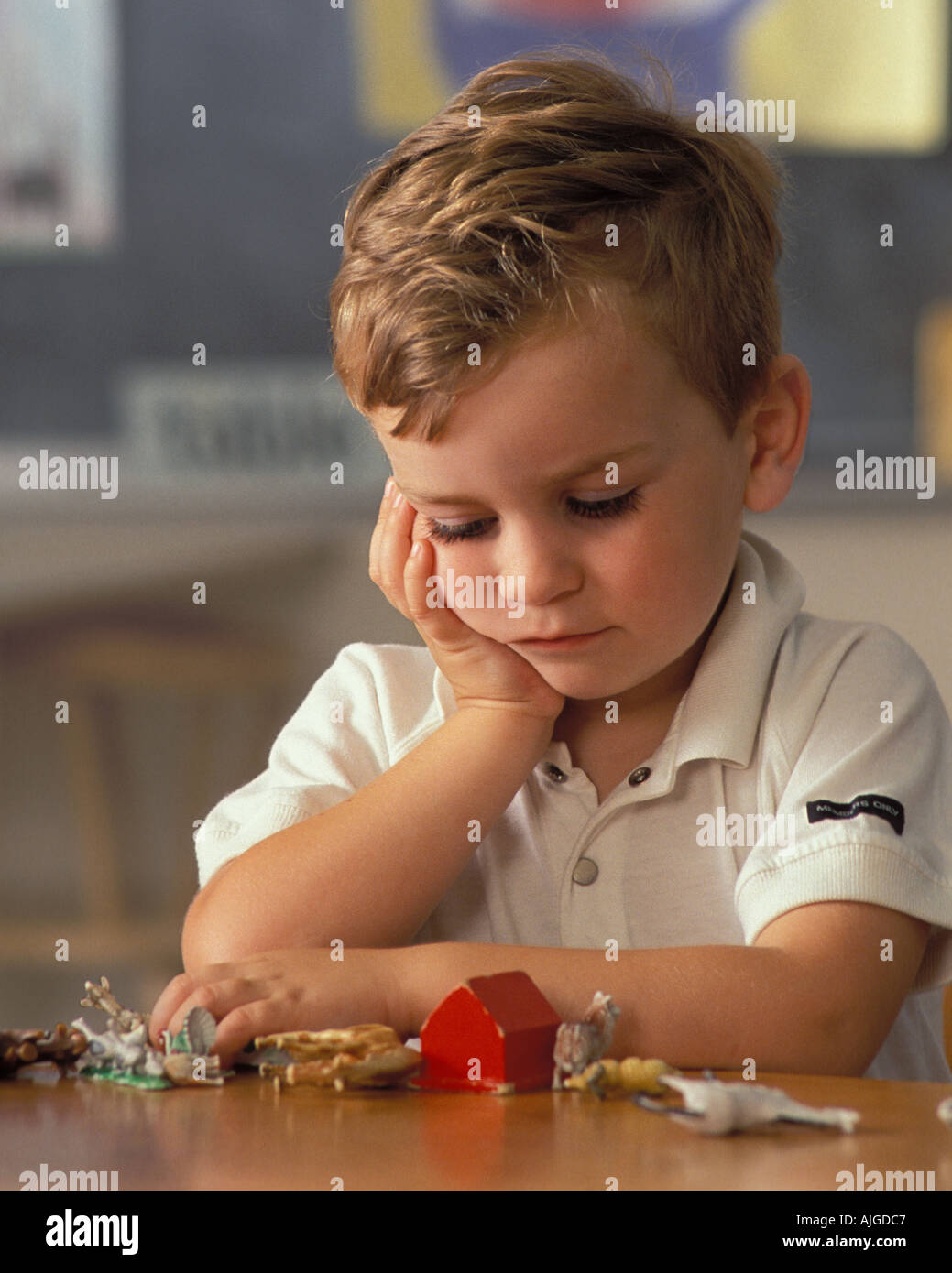 Sad looking Caucasian preschool male student playing with toy in class ...