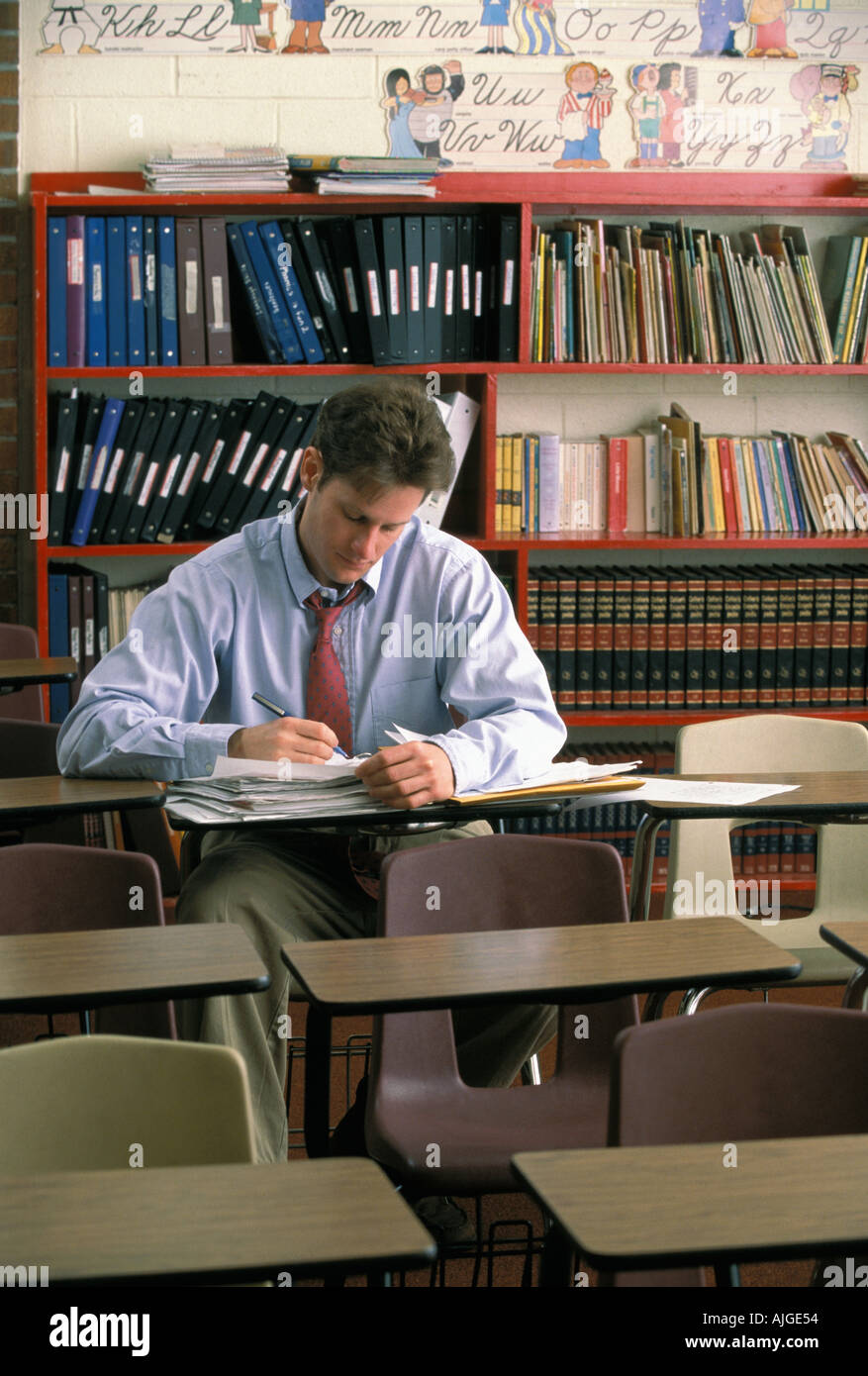Caucasian male teacher working alone on students papers after hours in ...