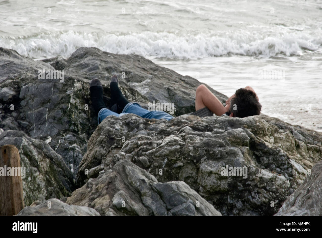 Young man laying on the rocks seaside Stock Photo - Alamy