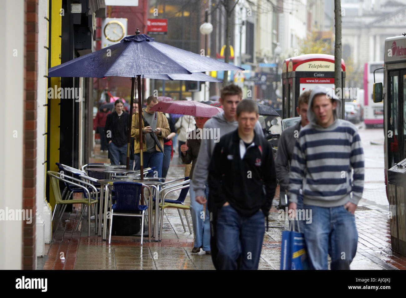 people walking past rain soaked parasols and outside dining tables and ...
