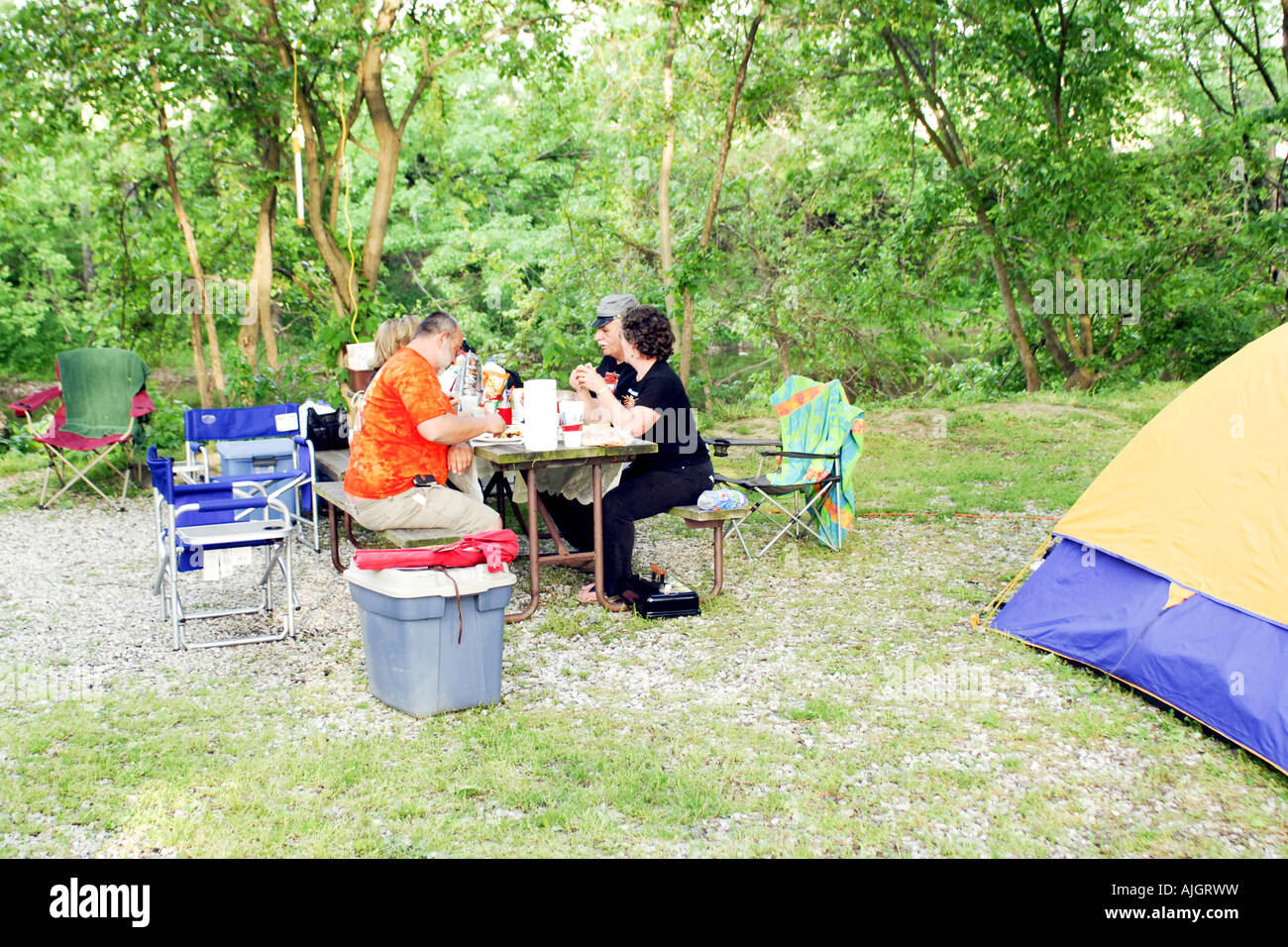 People sitting around a campsite picnic table having BBQ food and a ...