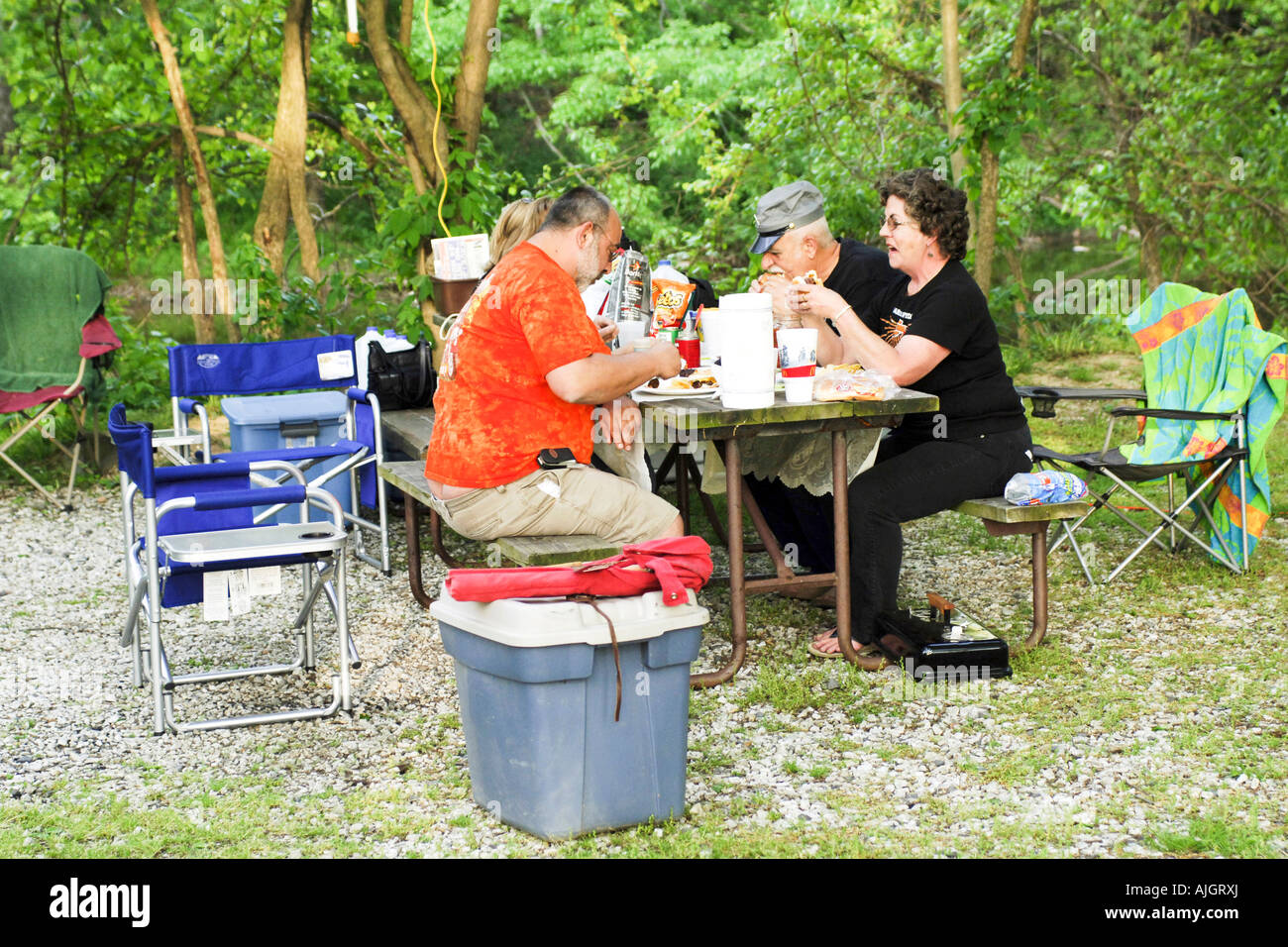 People sitting around a campsite picnic table having BBQ food and a ...