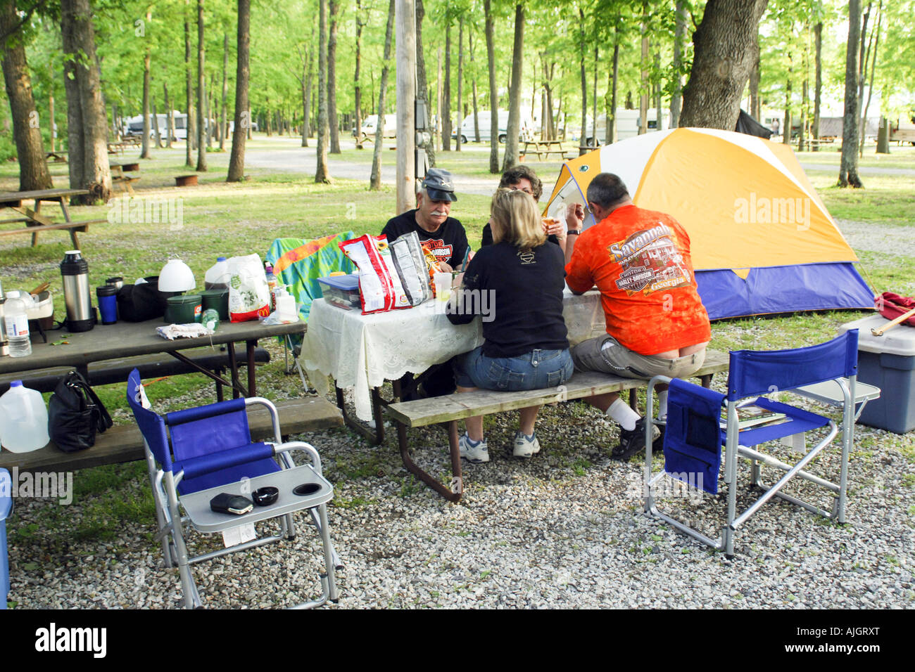 People sitting around a campsite picnic table having BBQ food and a ...