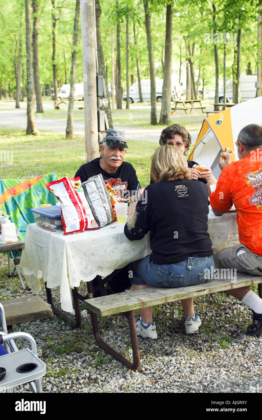 People sitting around a campsite picnic table having BBQ food and a ...