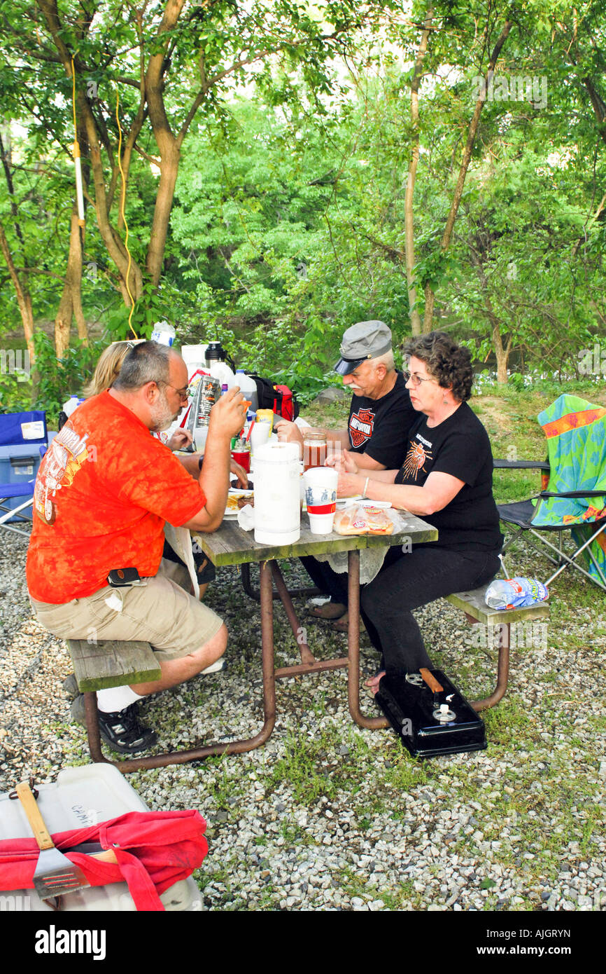 People sitting around a campsite picnic table having BBQ food and a ...