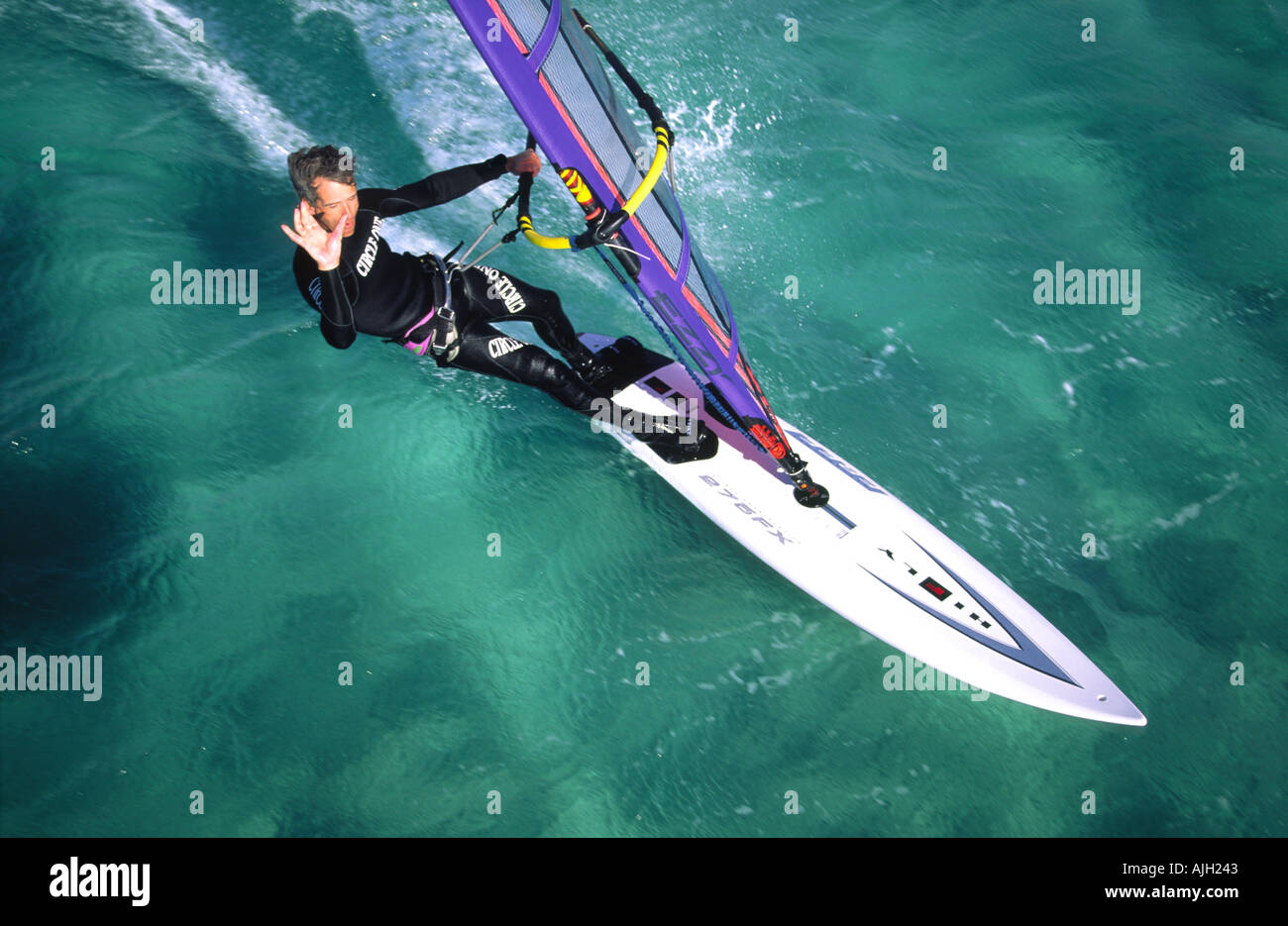 aerial panning shot of solo windsurfer sailing one handed waving on ...
