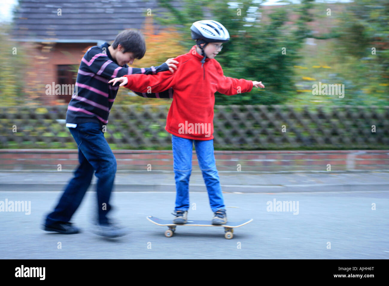a teenage boy is pushing his younger brother on a skateboard Stock ...