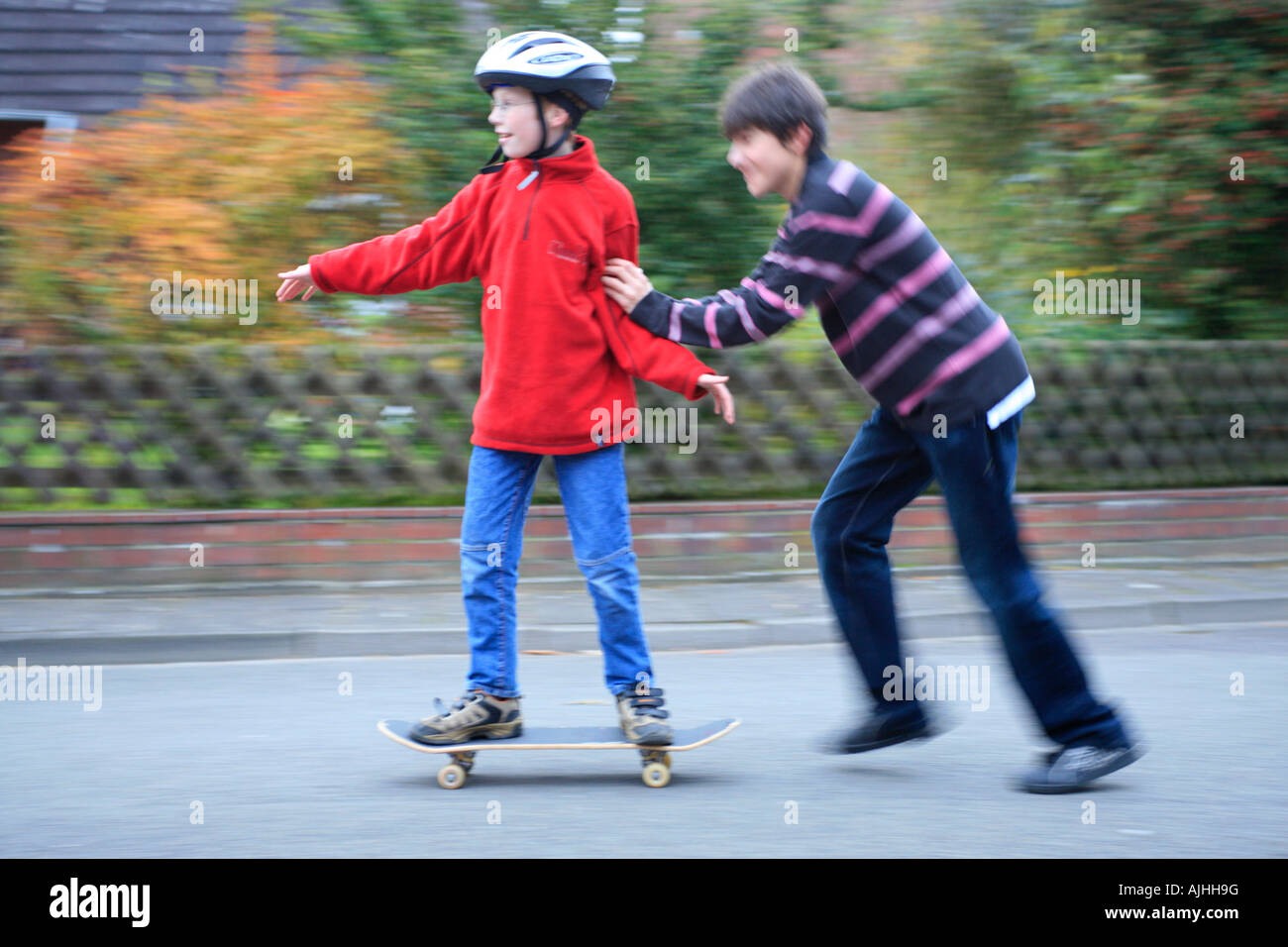 a teenage boy is pushing his younger brother on a skateboard Stock ...