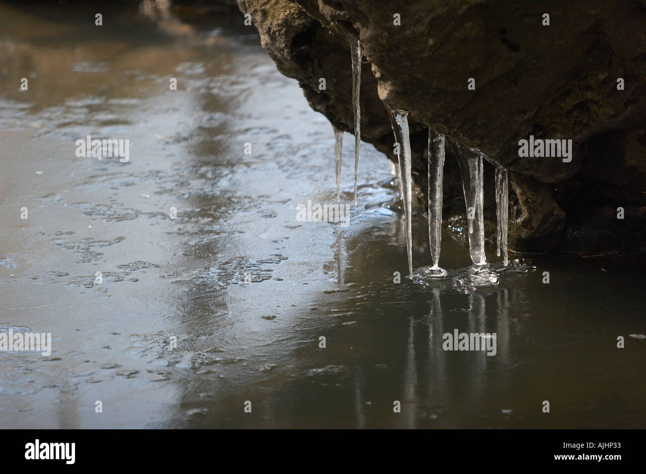 Icicles dripping down from a boulder to an icy river Stock Photo - Alamy