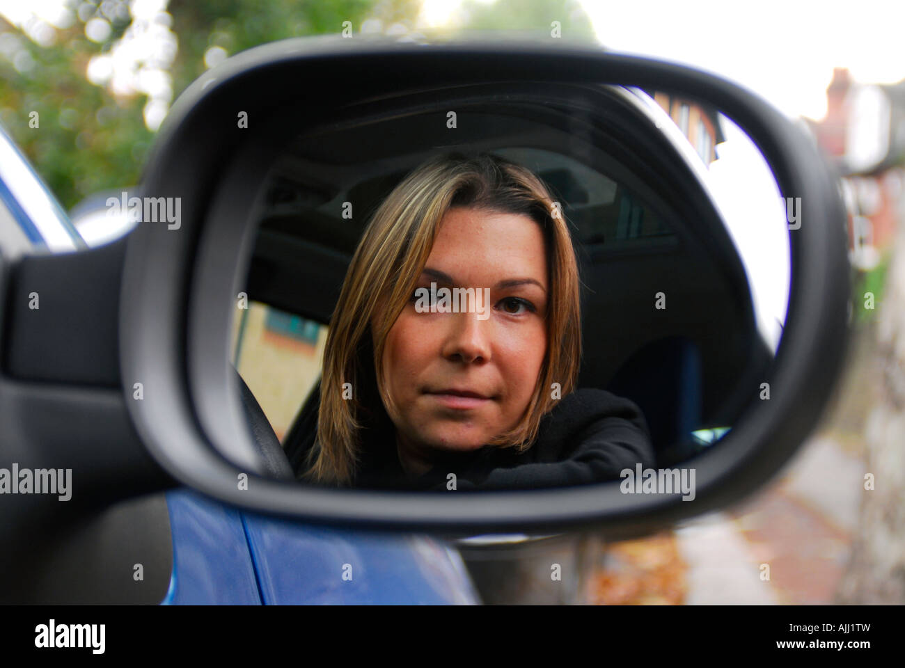 29 year old woman looking in rear view mirror of car, Chiswick, west ...