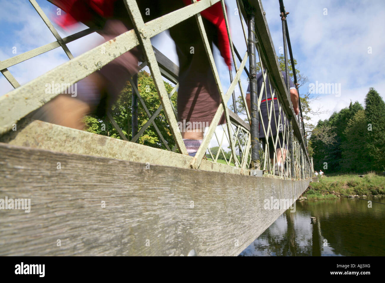 Walkers crossing the suspension footbridge over the River Wharfe near ...