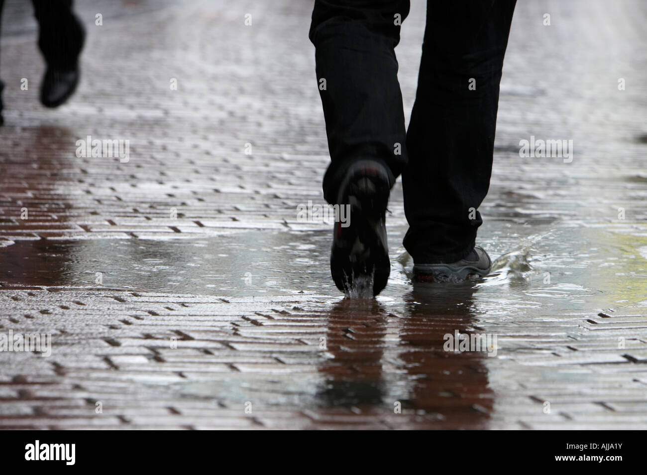 man walking through puddle of water pool in pedestrian area of belfast ...