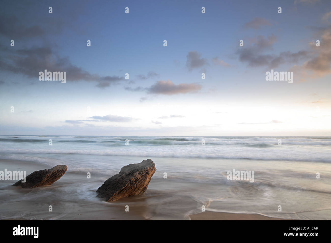 Beach scene at sunset with rocks Stock Photo - Alamy