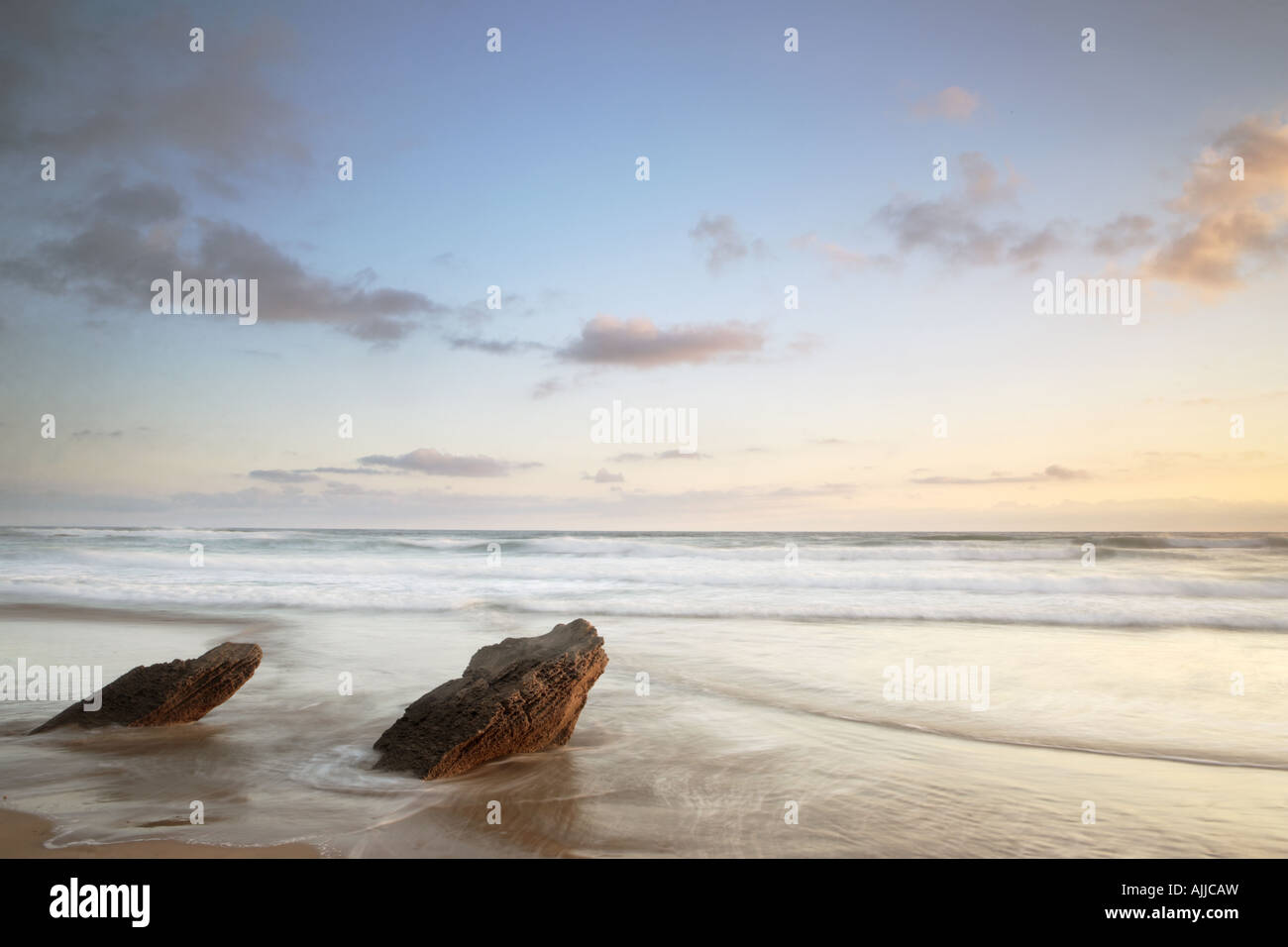 Beach scene at sunset with rocks Stock Photo - Alamy