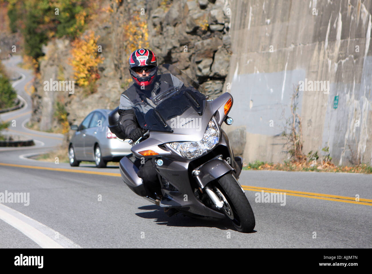 A silver sport touring motorcycle on a mountain road. A stone cliff and ...