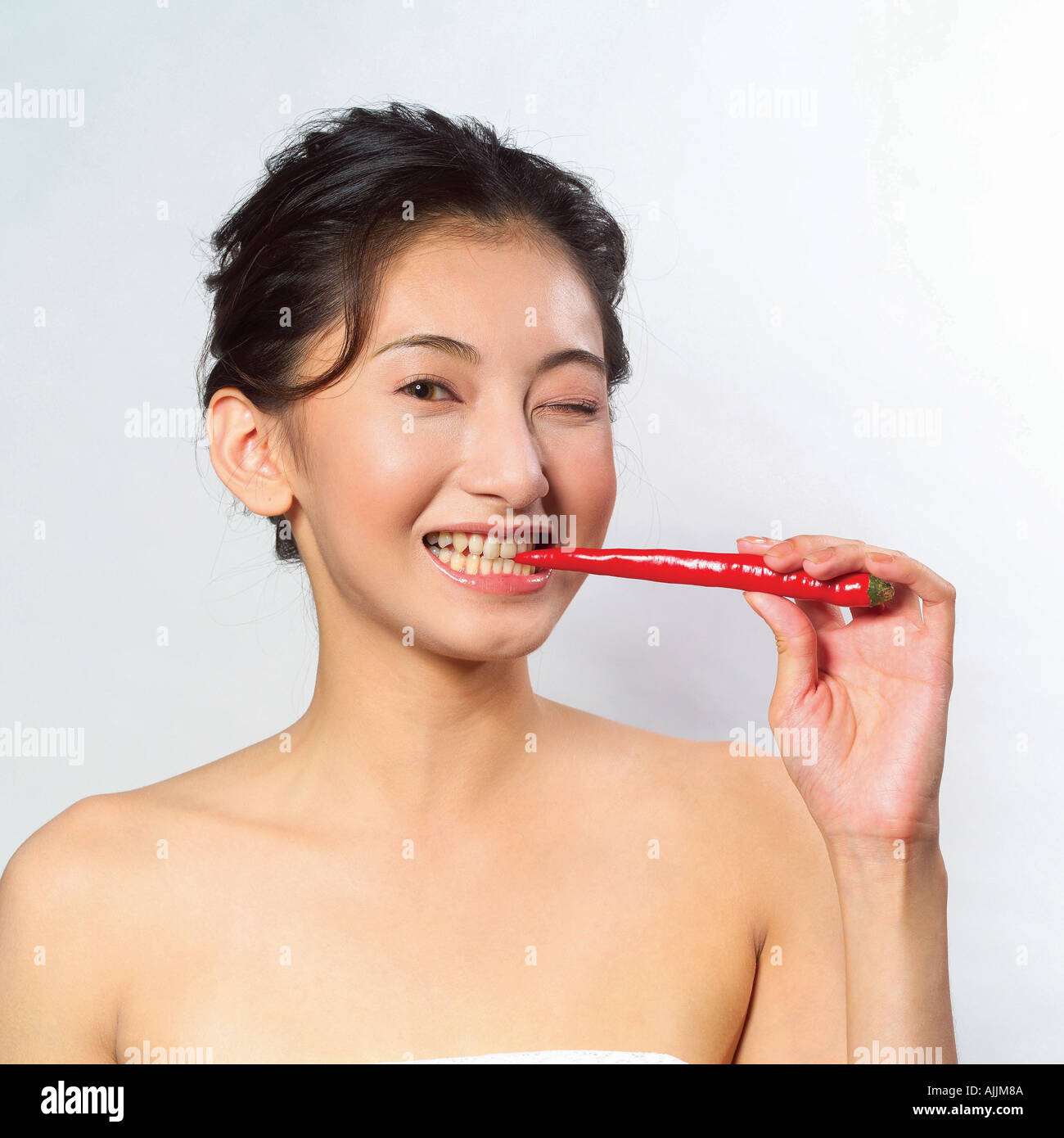 Portrait of a young woman biting into a red chilli Stock Photo - Alamy