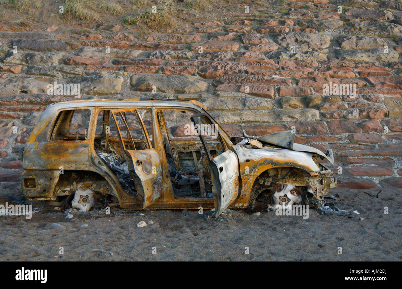 Rusty burnt out car shell on beach with stonewall in background uk ...