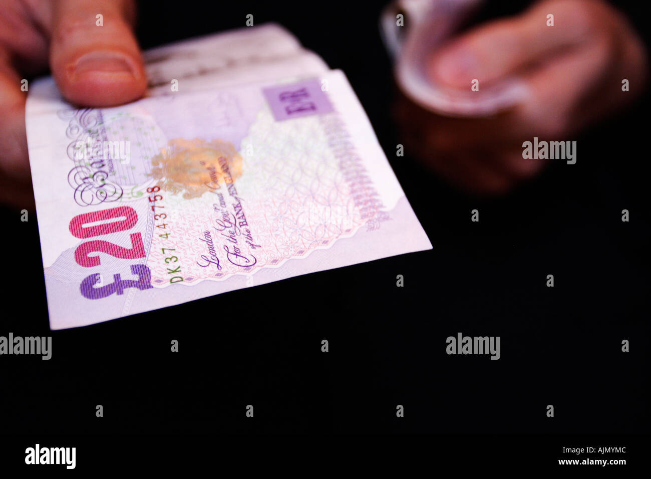 A man hands over a twenty british pound note from a bundle of cash ...