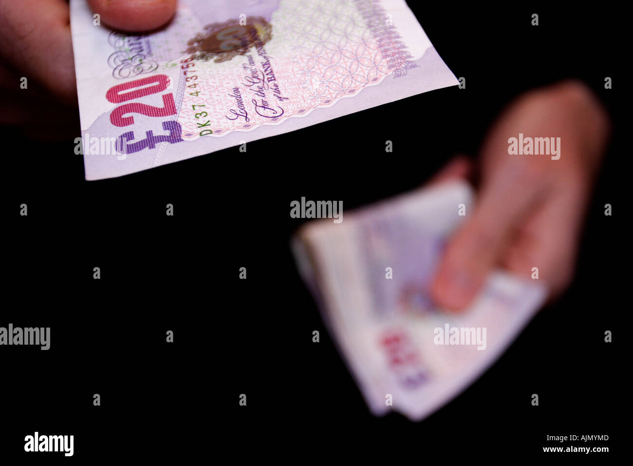 A man hands over a twenty british pound note from a bundle of cash ...