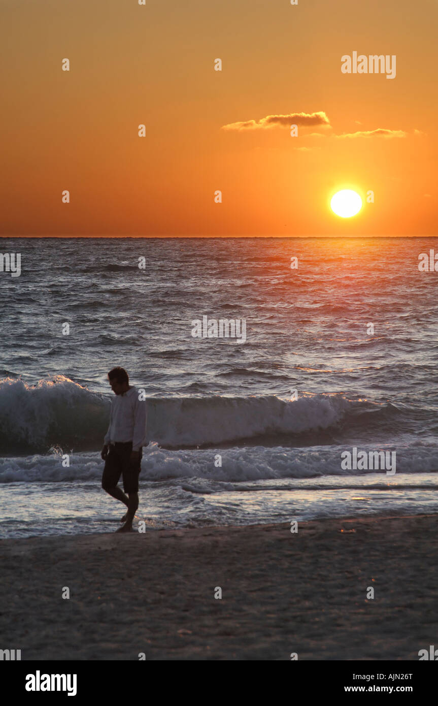 single man male walking along beach with waves crashing behind sunset ...