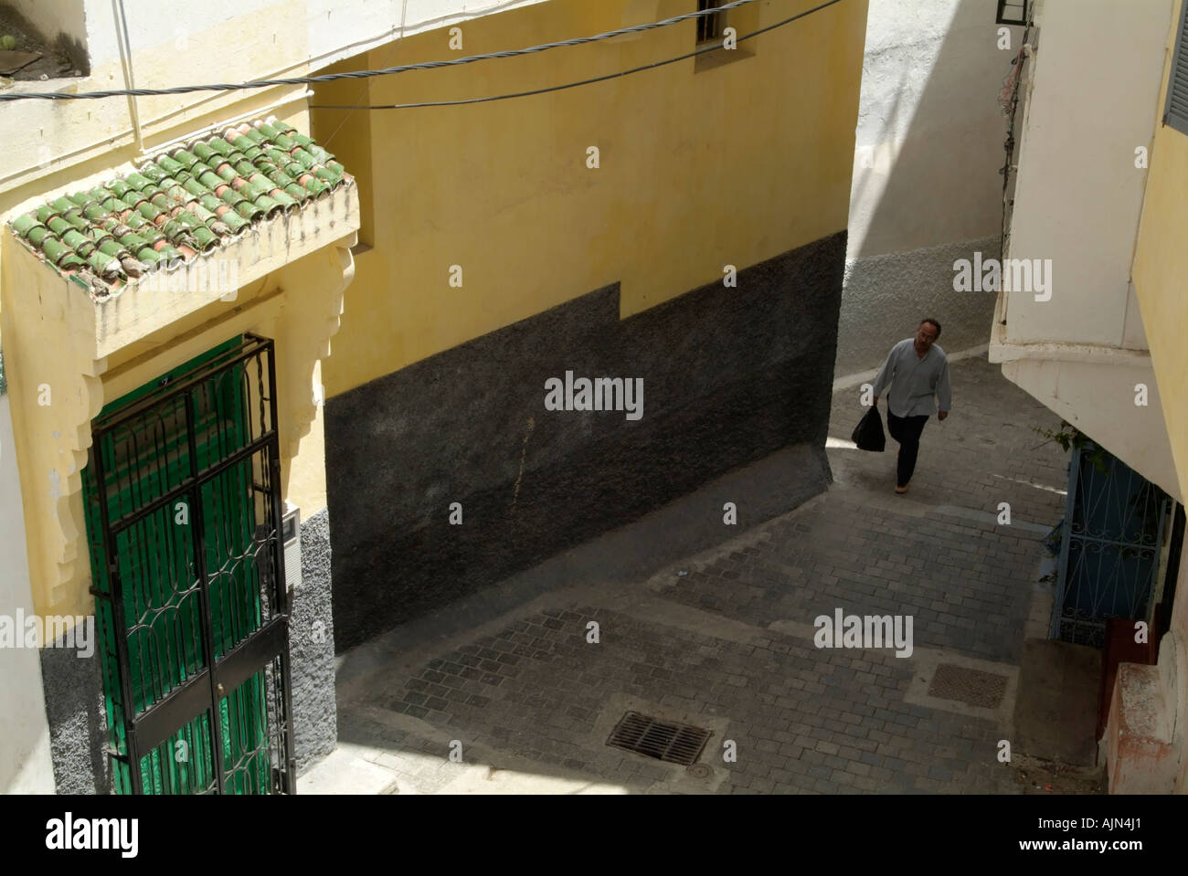A man climbs shallow steps carrying a triangular black bag in an alley ...