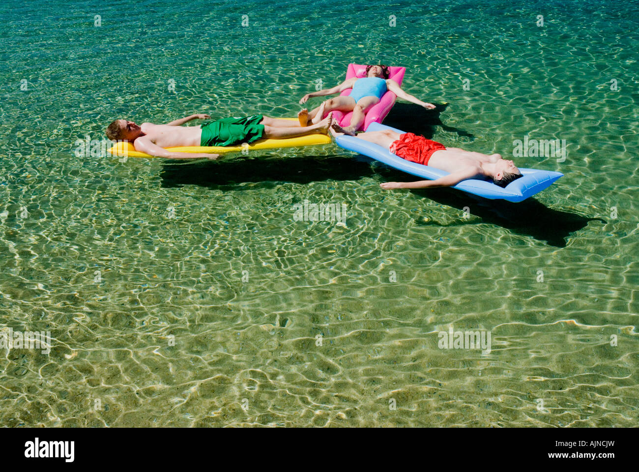 Three people floating on li los inflatable airbeds blue sea and sky ...