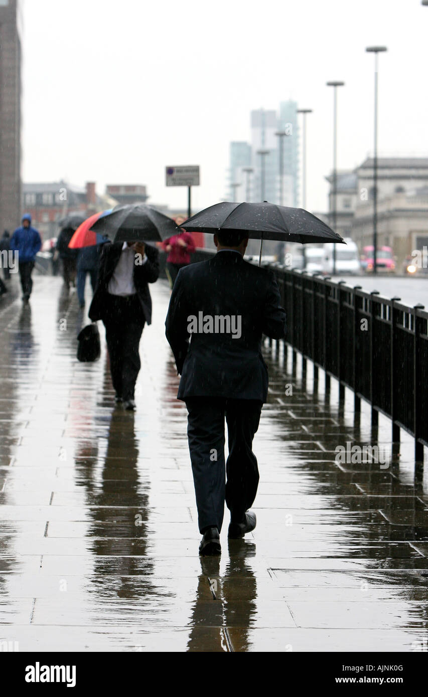 Businessmen walk to work over London Bridge in the rain with umbrellas ...
