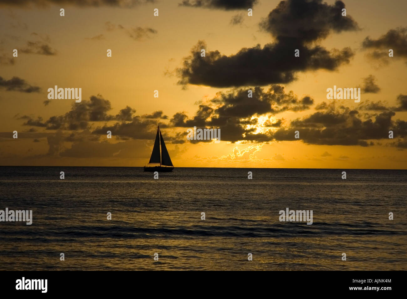 Sailboat silhouetted against the setting sun off the Caribbean Island ...