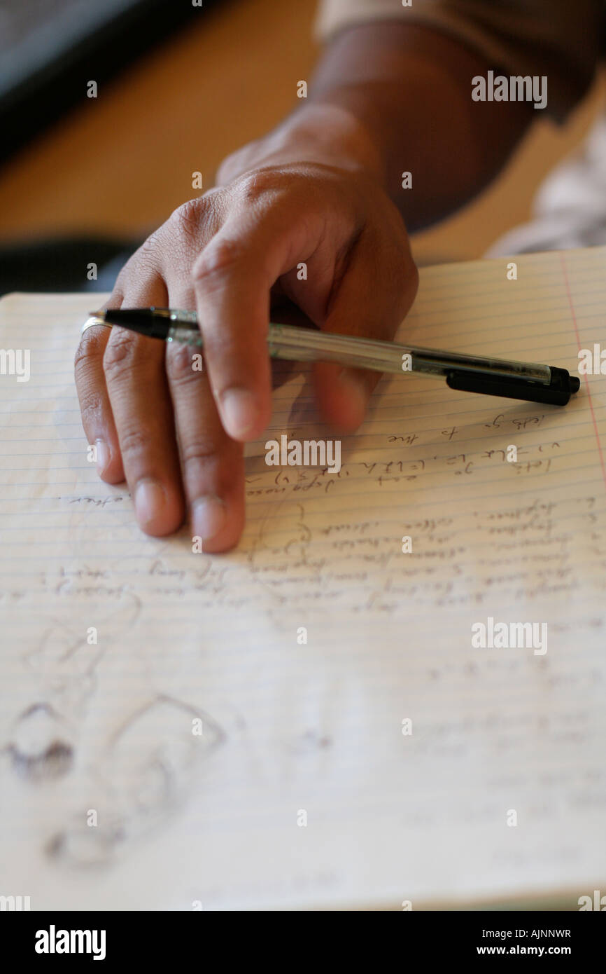 Hand with pen resting on an open notepad with writing and some drawing ...