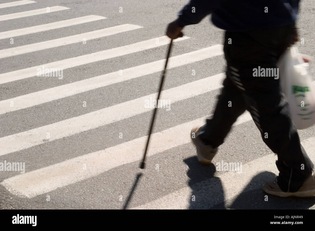 Close up of legs and feet with a hand holding a cane crossing a street ...