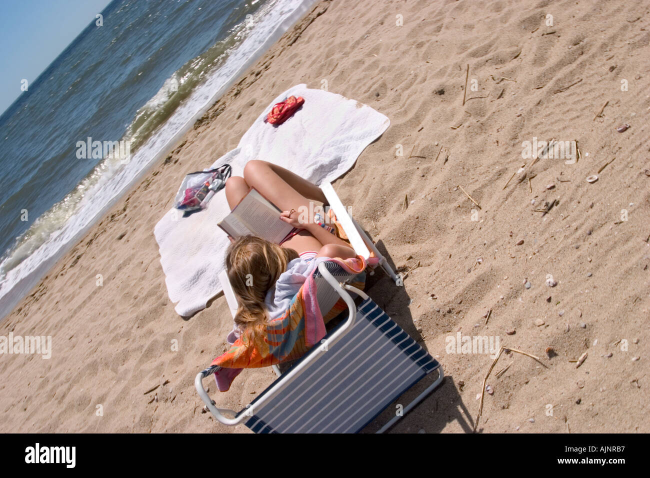 Young woman at the beach sitting on a folding chair reading a book ...