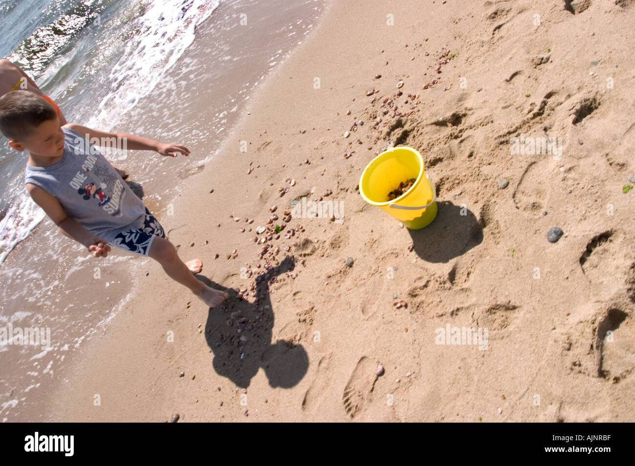 Young boy at the beach with a yellow bucket looking for sea shells ...