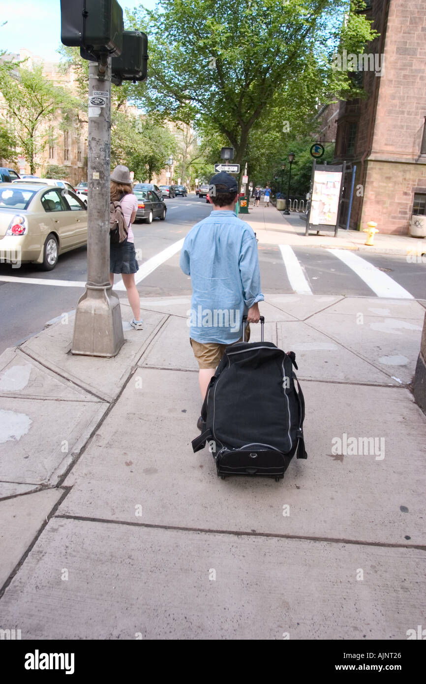 Teen boy walking down a city street pulling a suitcase that is on ...