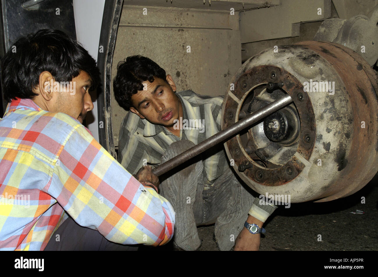Two indian men repairing dismantled broken bus wheel at night outdoors ...