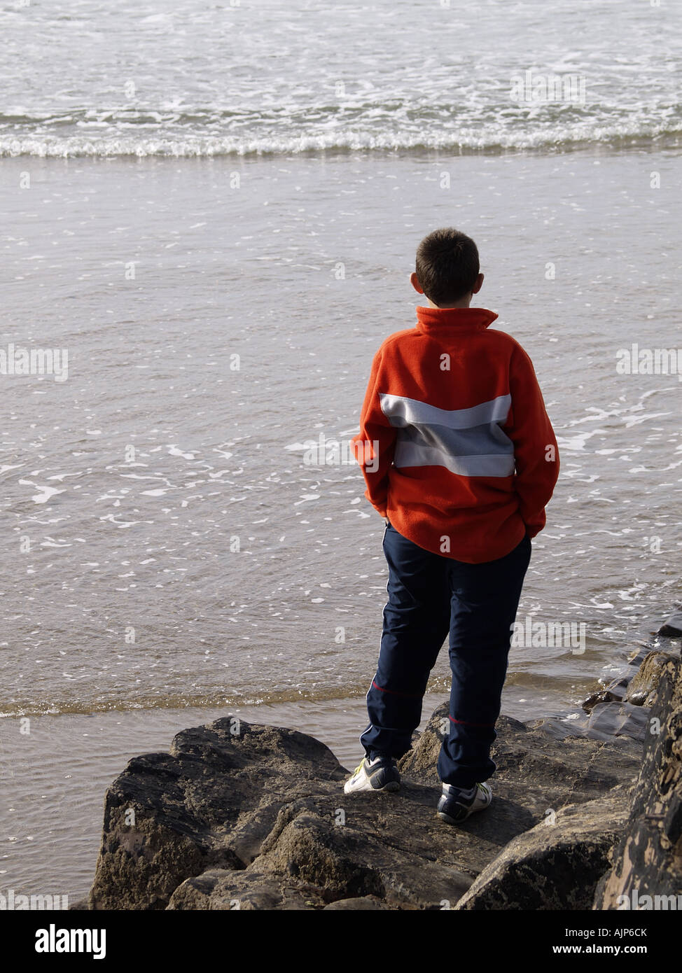 Teenage boy standing on rock looking out at the sea Stock Photo - Alamy