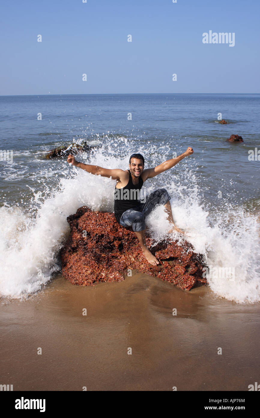 Man sitting on rock with waves crashing Stock Photo - Alamy