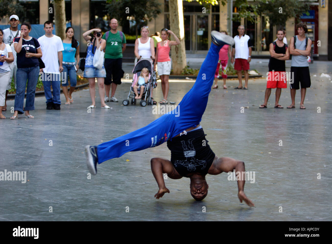 Black man dancer performs on a street - balances on hands with feet up ...