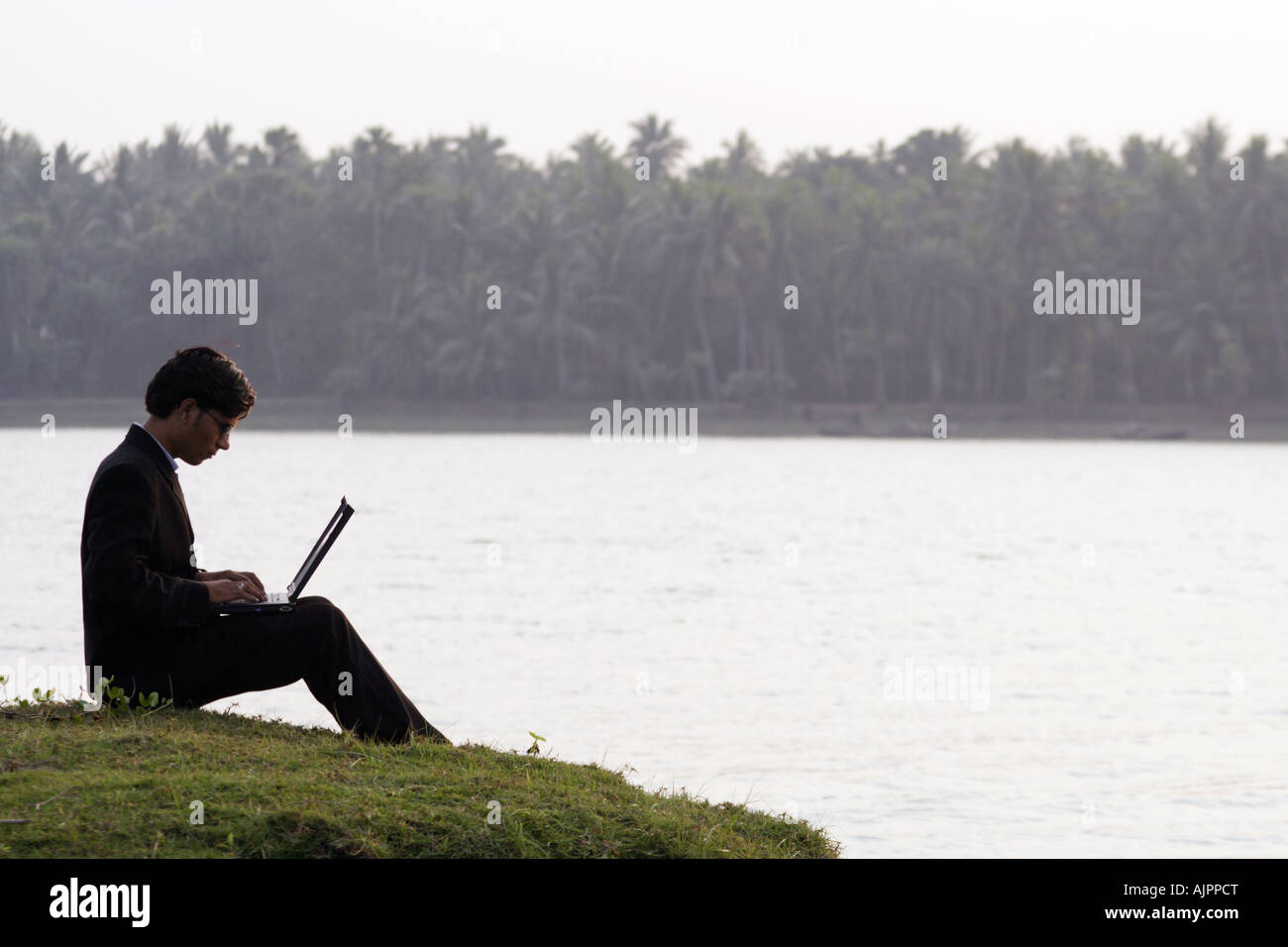 An executive sitting by a river with his laptop Stock Photo - Alamy