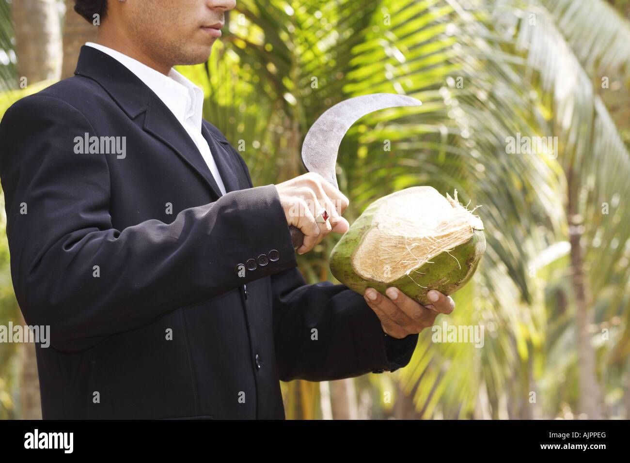 A well dressed man using a sickle to cut open a coconut Stock Photo - Alamy