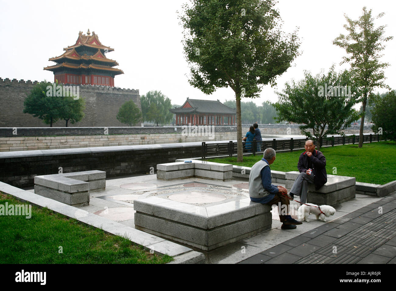 People sitting at the north moat park by the wall surrounding the ...