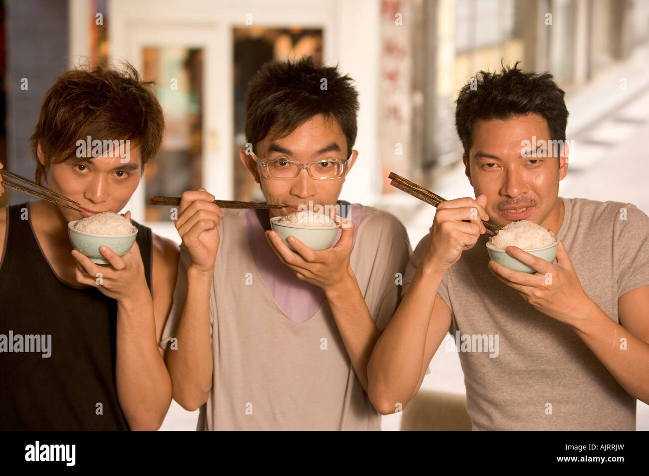 Portrait of three young men eating rice with chopsticks Stock Photo - Alamy