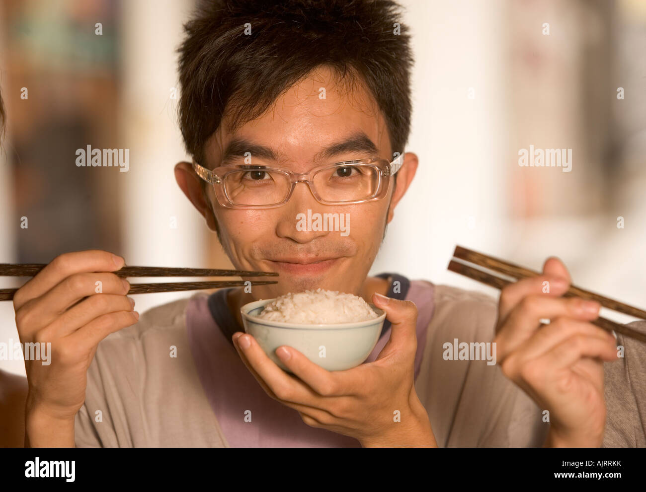 Portrait of a young man holding a bowl of white rice and a pair of ...