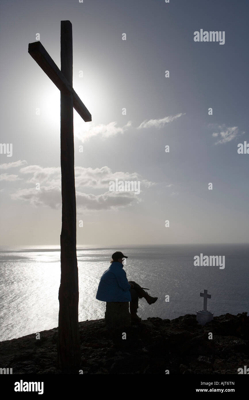 Woman is sitting in front of a wodden crux near the lighthouse Faro the ...