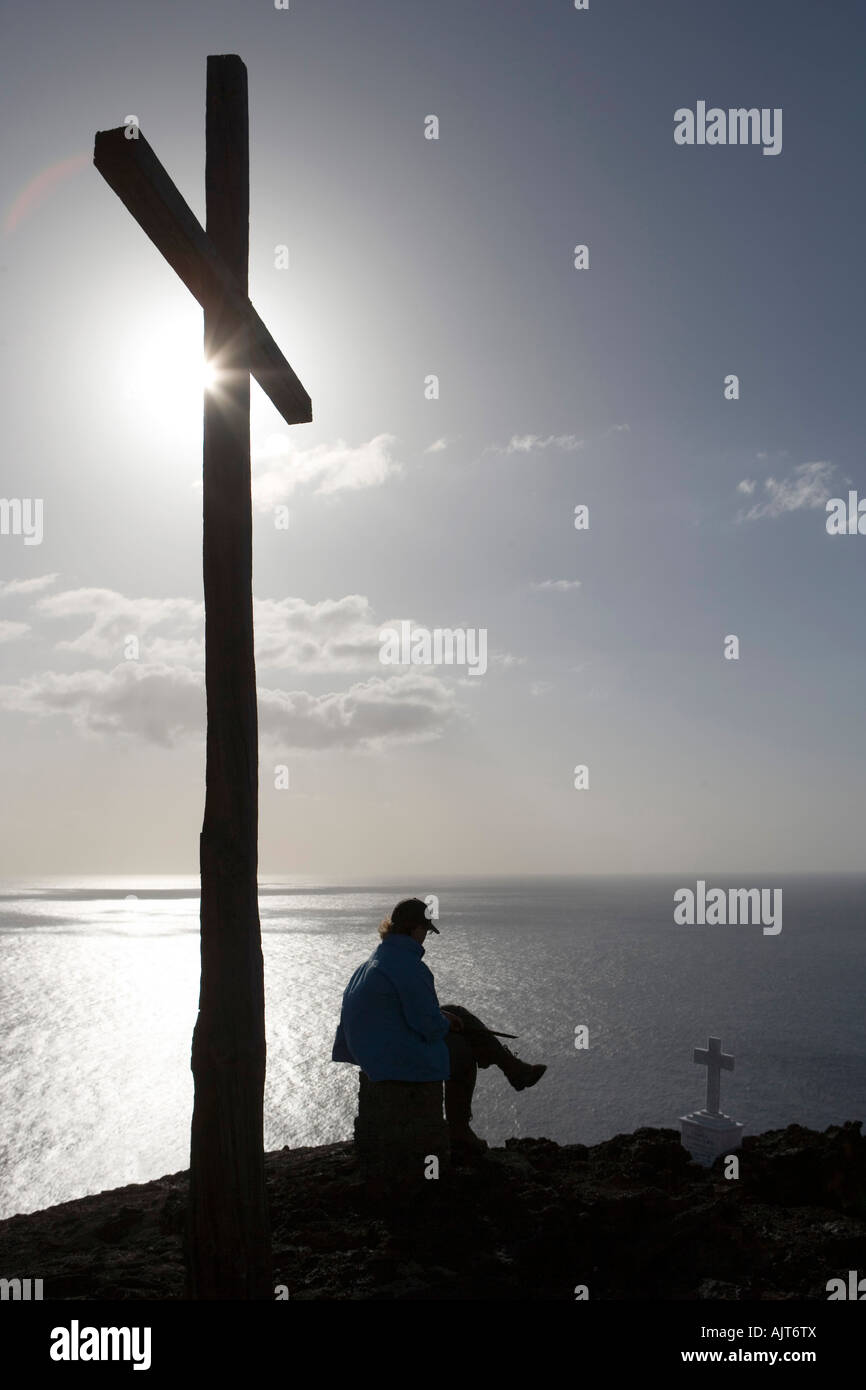 Woman is sitting in front of a wodden crux near the lighthouse Faro the ...